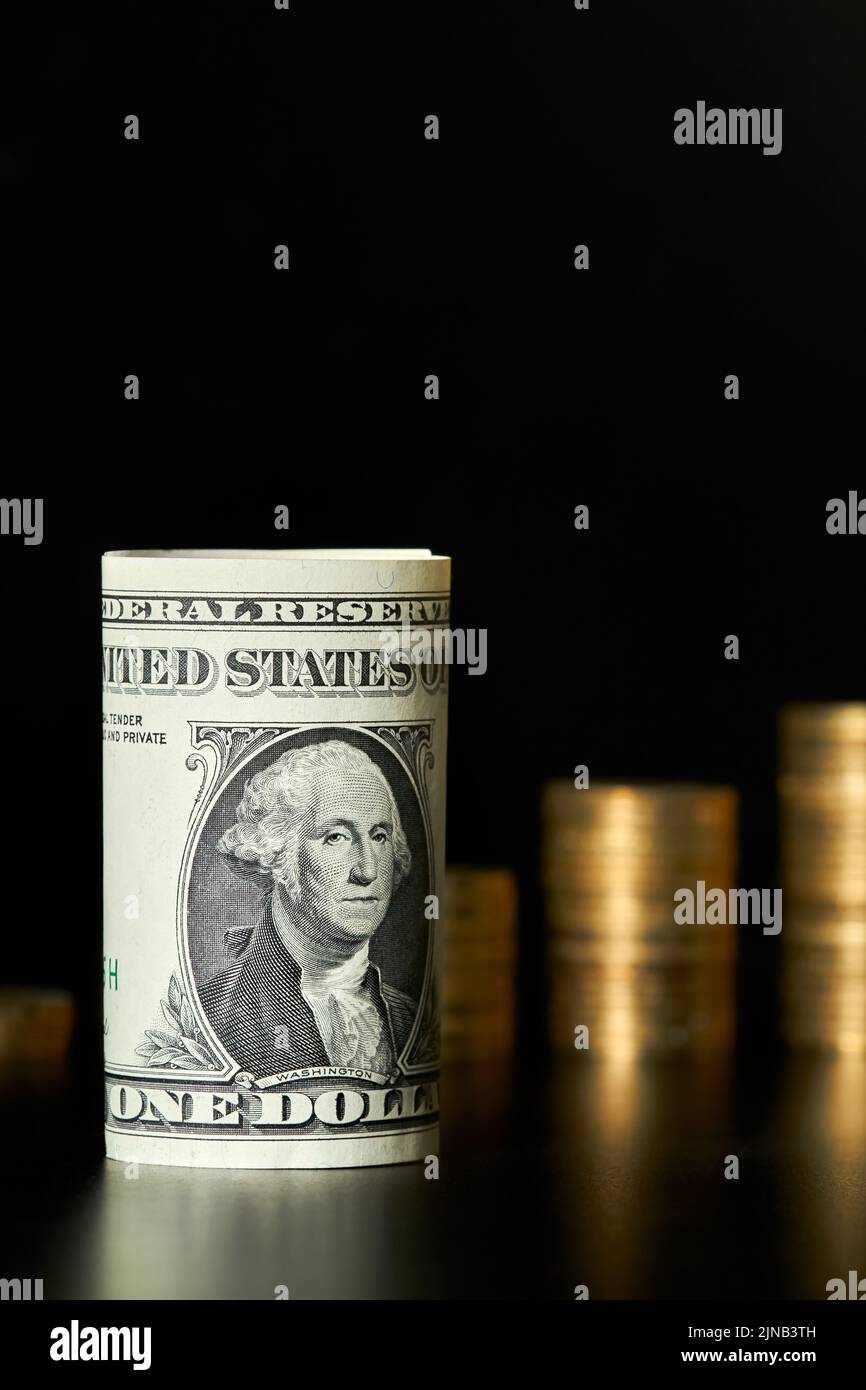 Rolled one dollar bill on the background of stacks of coins Stock Photo ...