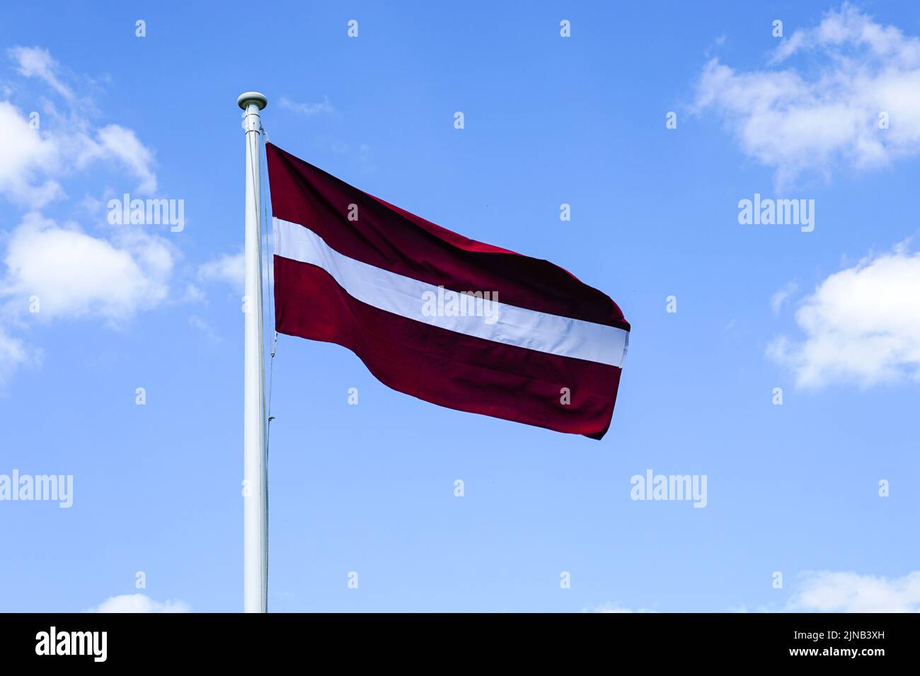 Latvian State Flag on the mast waving in the wind against blue sky with white clouds Stock Photo ...