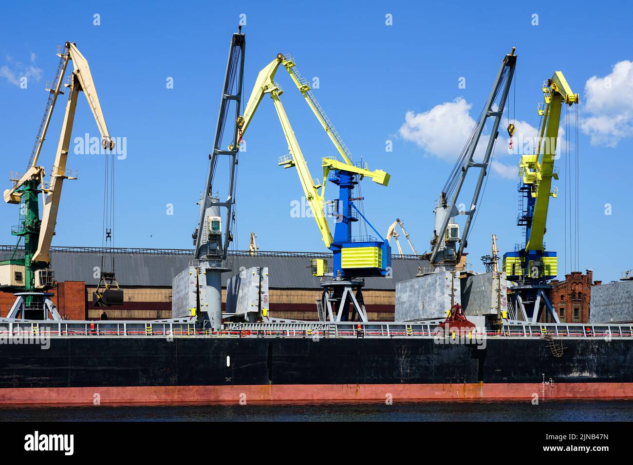 Yellow and blue painted cranes are loading bulk carriers in the port ...