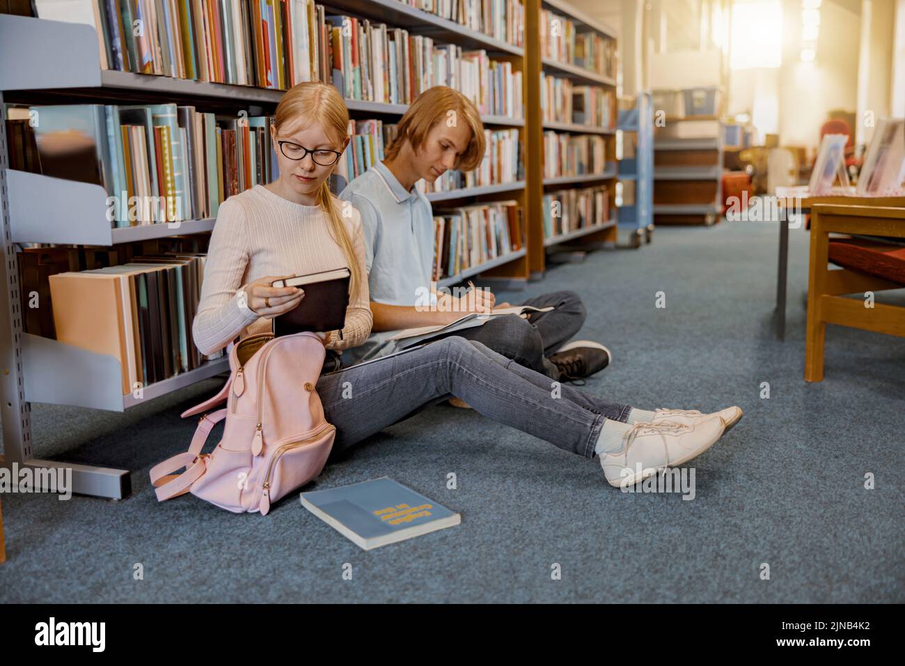 Friends student sit on floor near bookshelves in library and studying ...