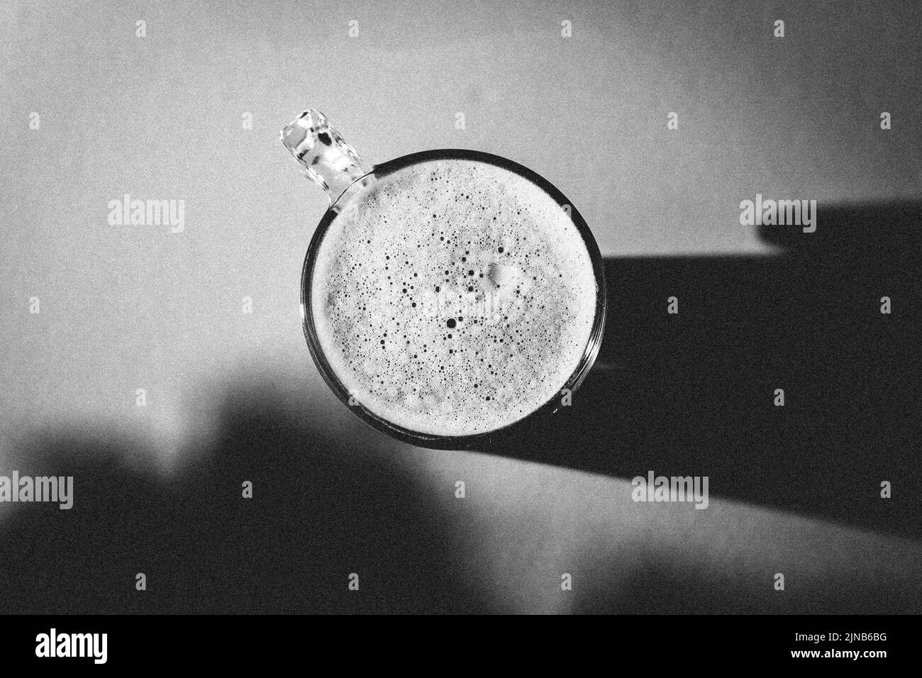 A top view of a full coffee glass with foam on the surface, greyscale ...