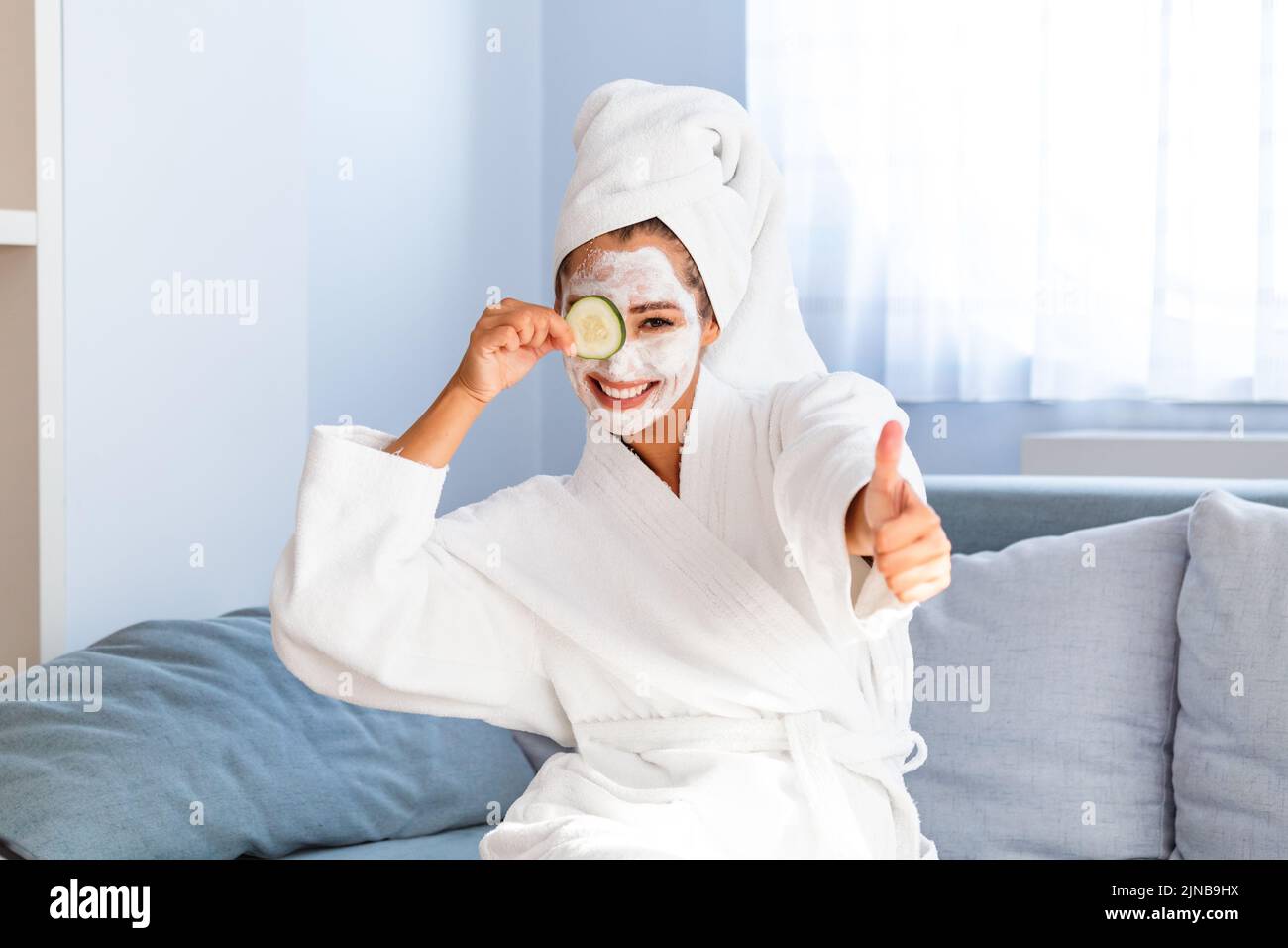Young woman with clay facial mask holding cucumber slices. Beautiful young woman with facial ...