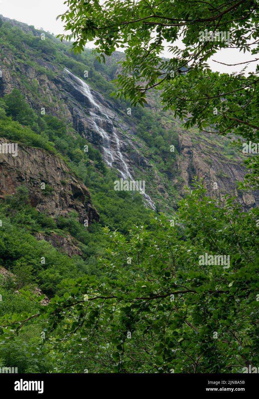 a waterfall and river pour through steep-sided rock gorge with white ...