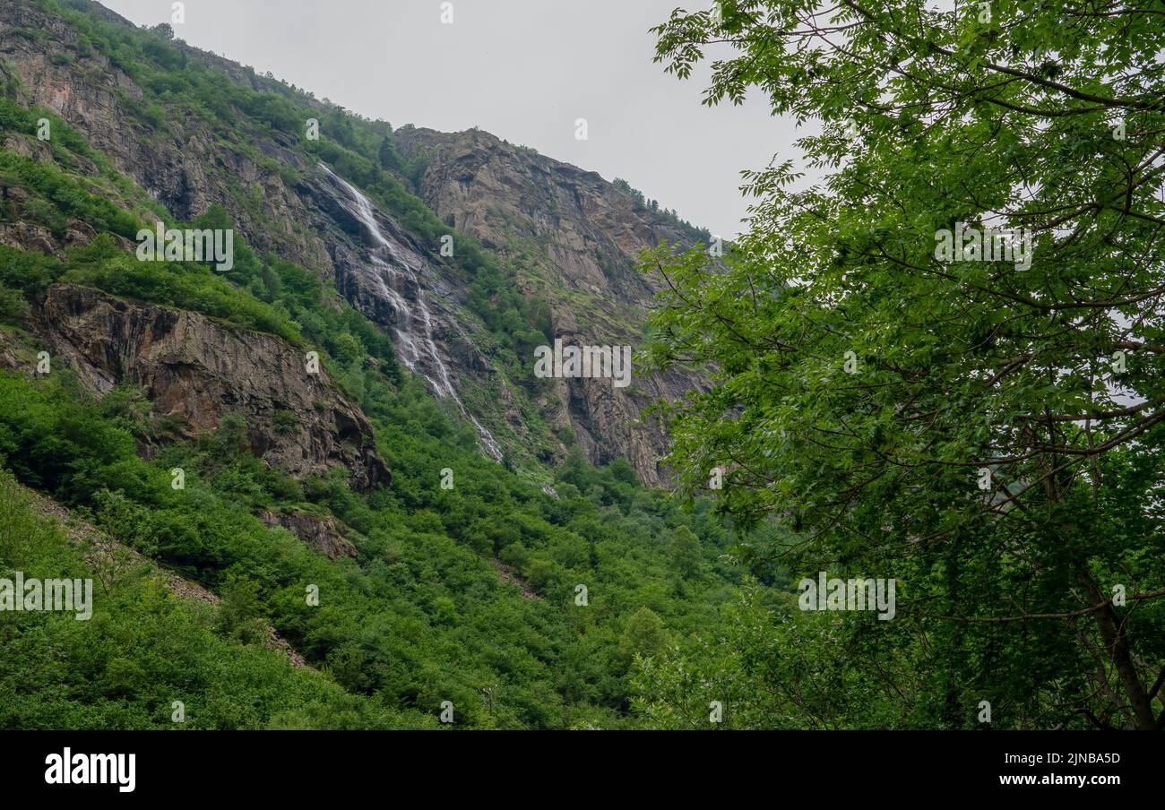 a waterfall and river pour through steep-sided rock gorge with white ...