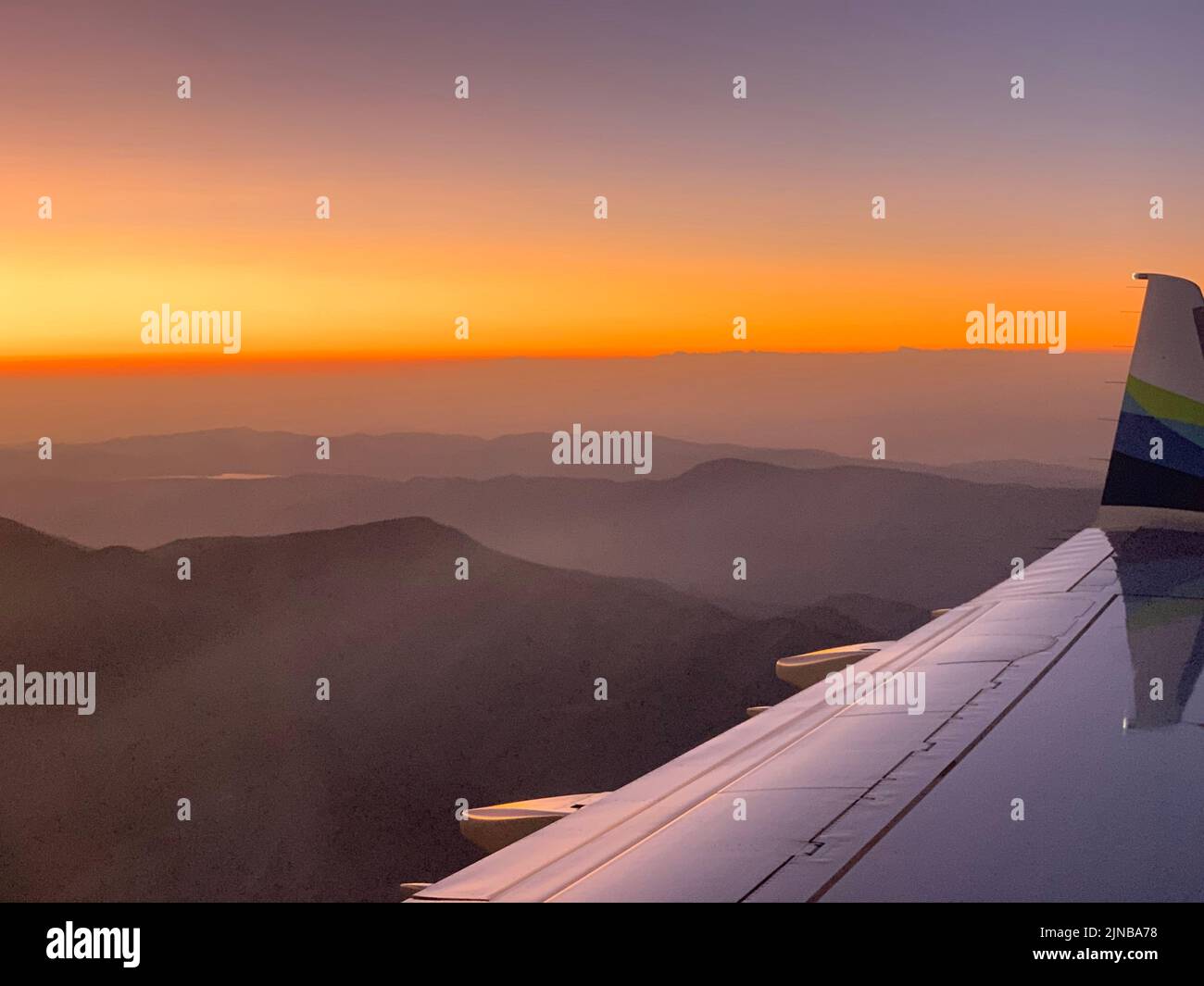 A vivid orange sunset and an airplane wing captured during the flight ...