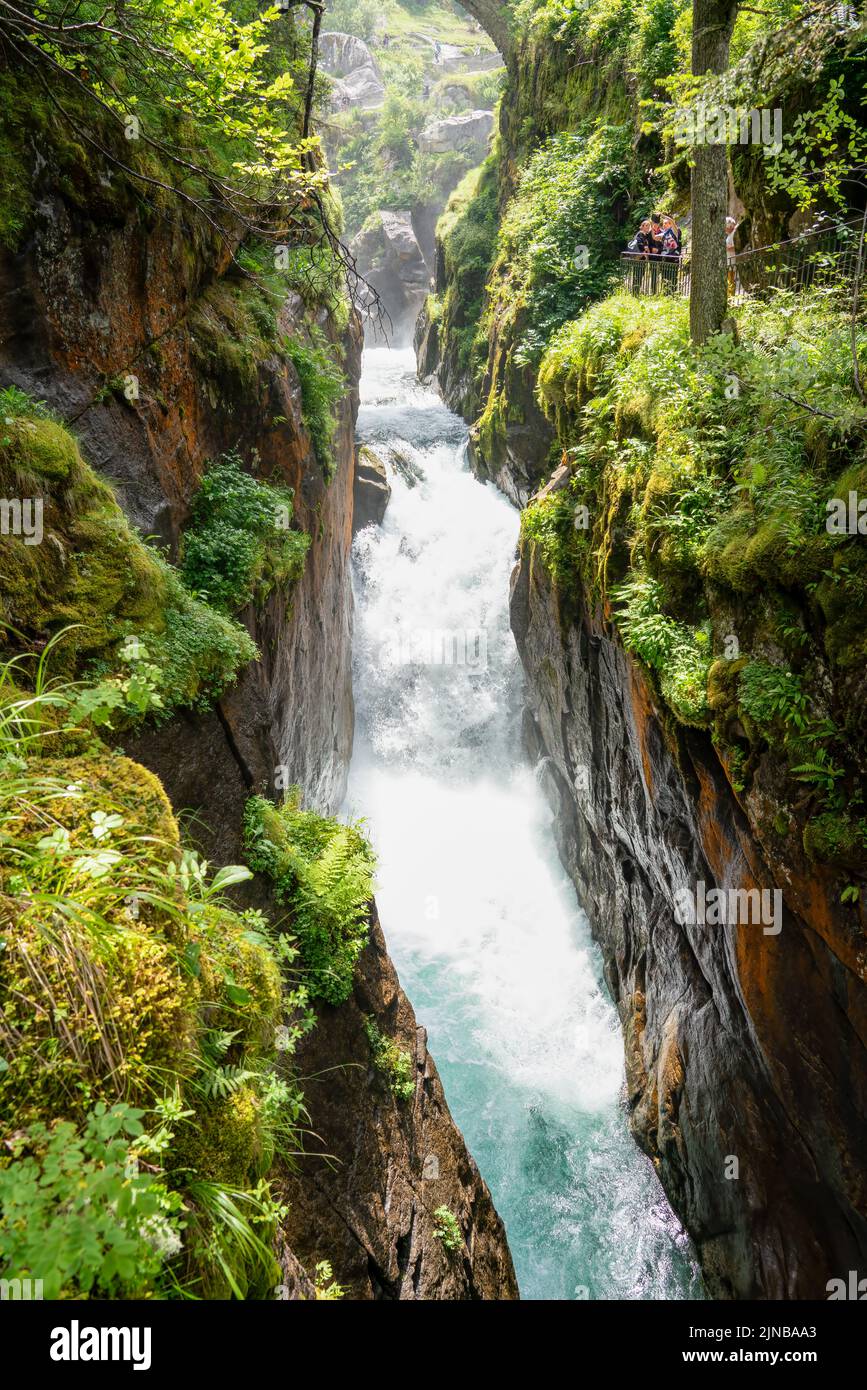 a waterfall and river pour through steep-sided rock gorge with white ...