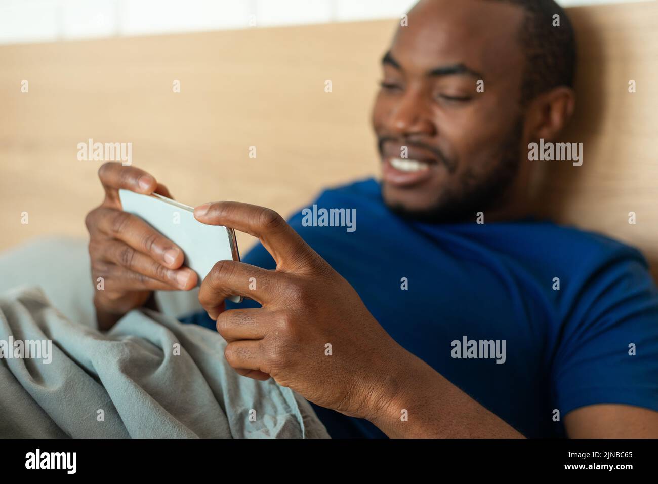 Black Male Using Smartphone Playing Mobile Games Lying In Bedroom Stock ...