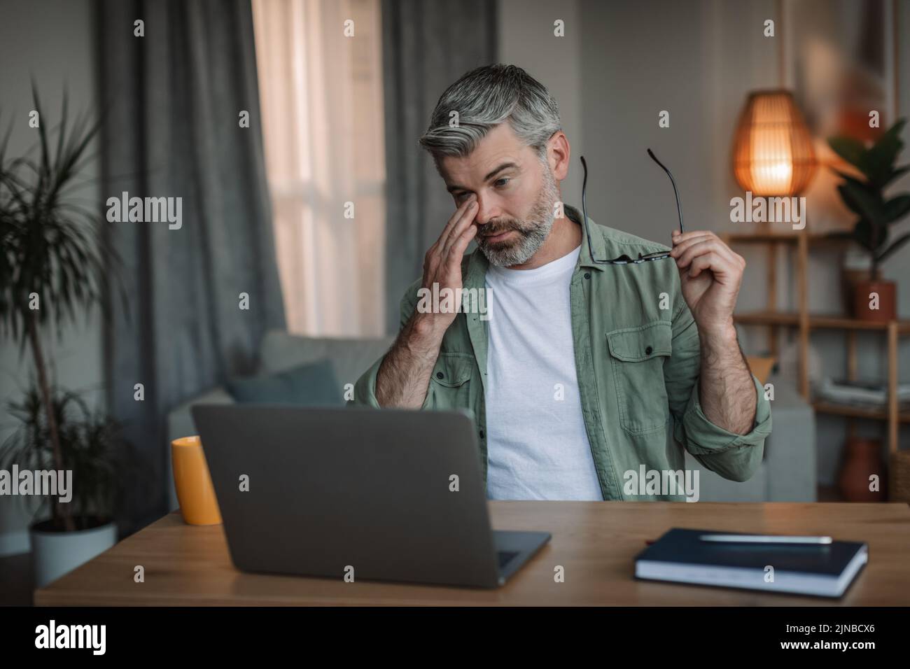 Sad tired retired caucasian man with beard takes off his glasses, rubs ...