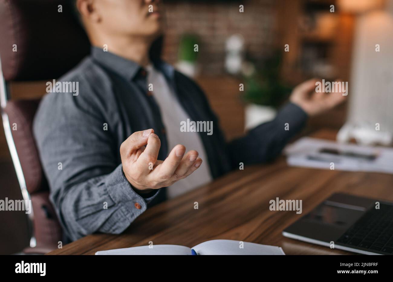Serious calm adult japanese male resting in chair at table with laptop ...