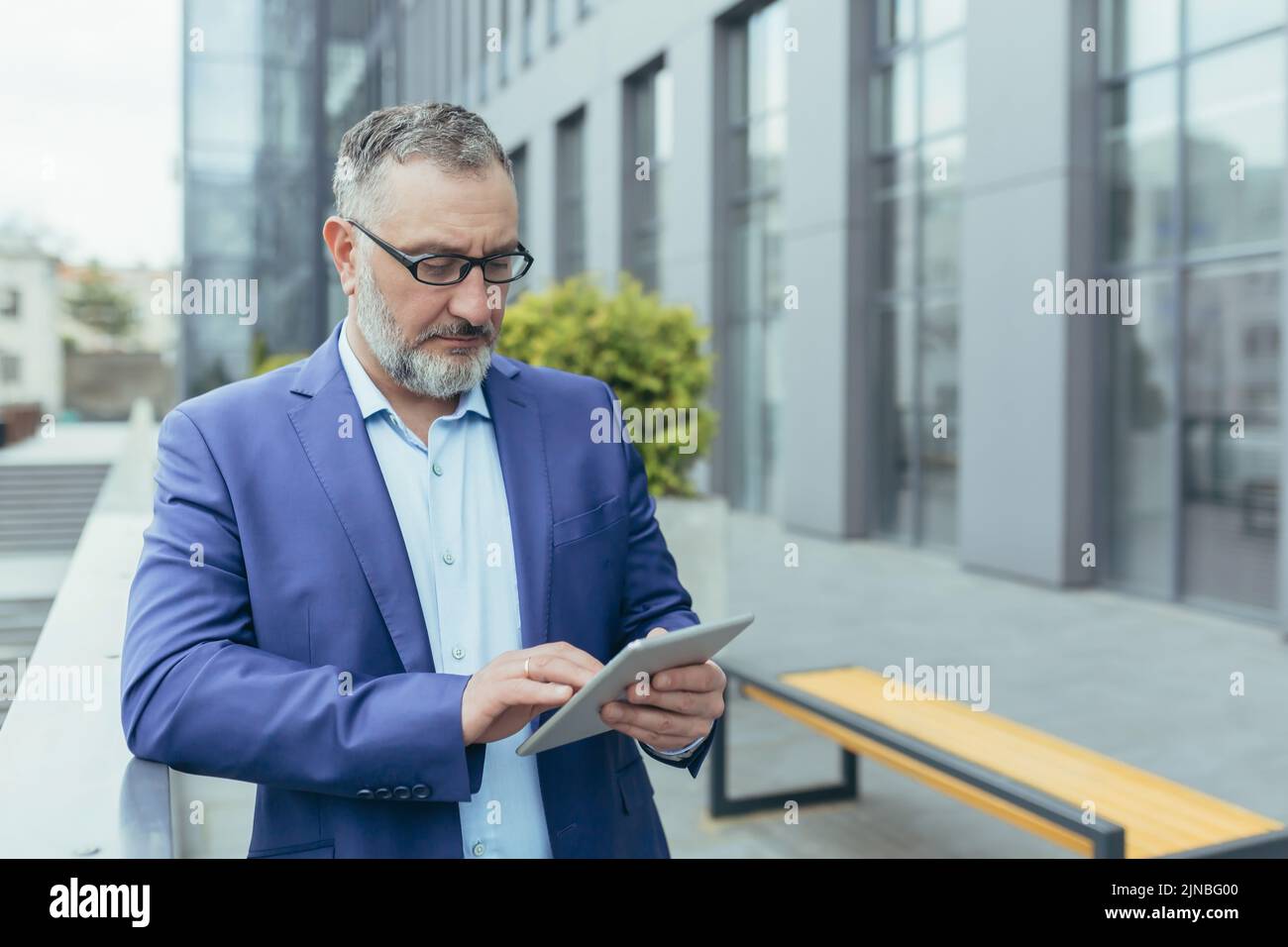 Concentrated and serious senior gray-haired banker using tablet ...
