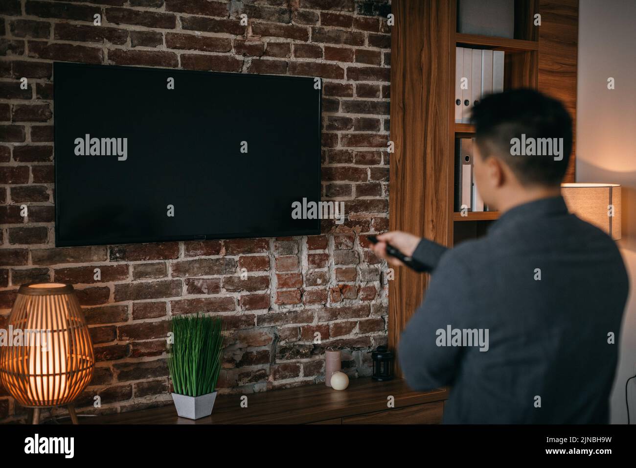 Adult chinese man with remote control turns on tv with blank screen in ...