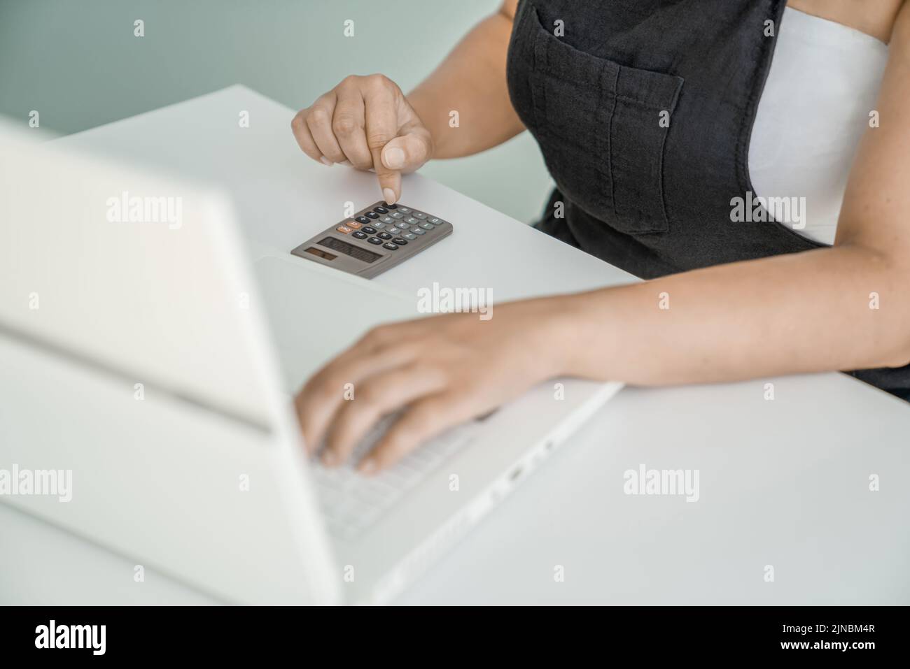 Young woman is sitting at her laptop and doing calculations on ...
