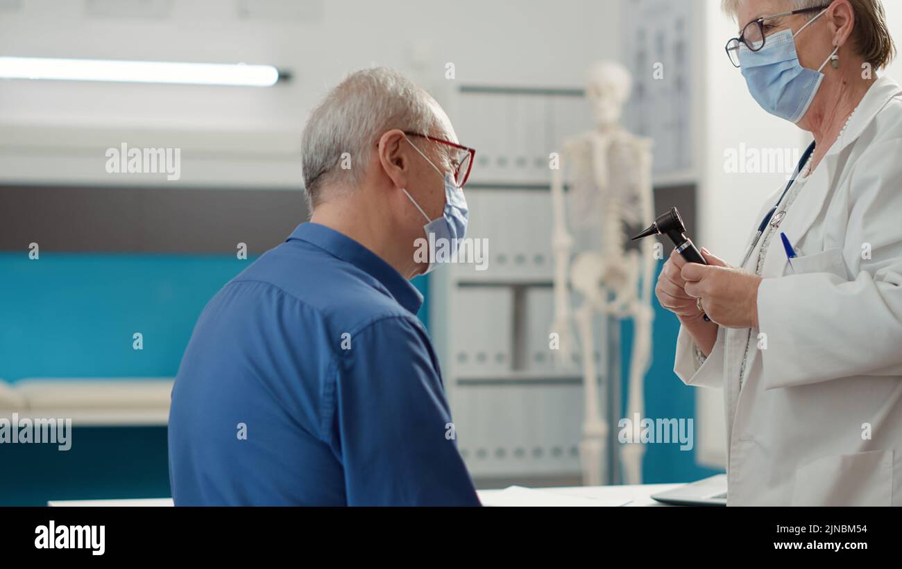Senior physician doing ear examination with otoscope, consulting ...