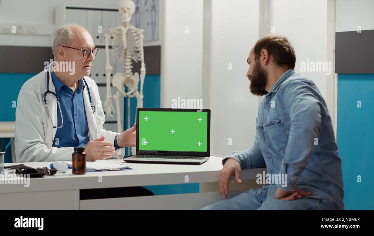 Doctor and young patient using laptop with greenscreen on office desk ...