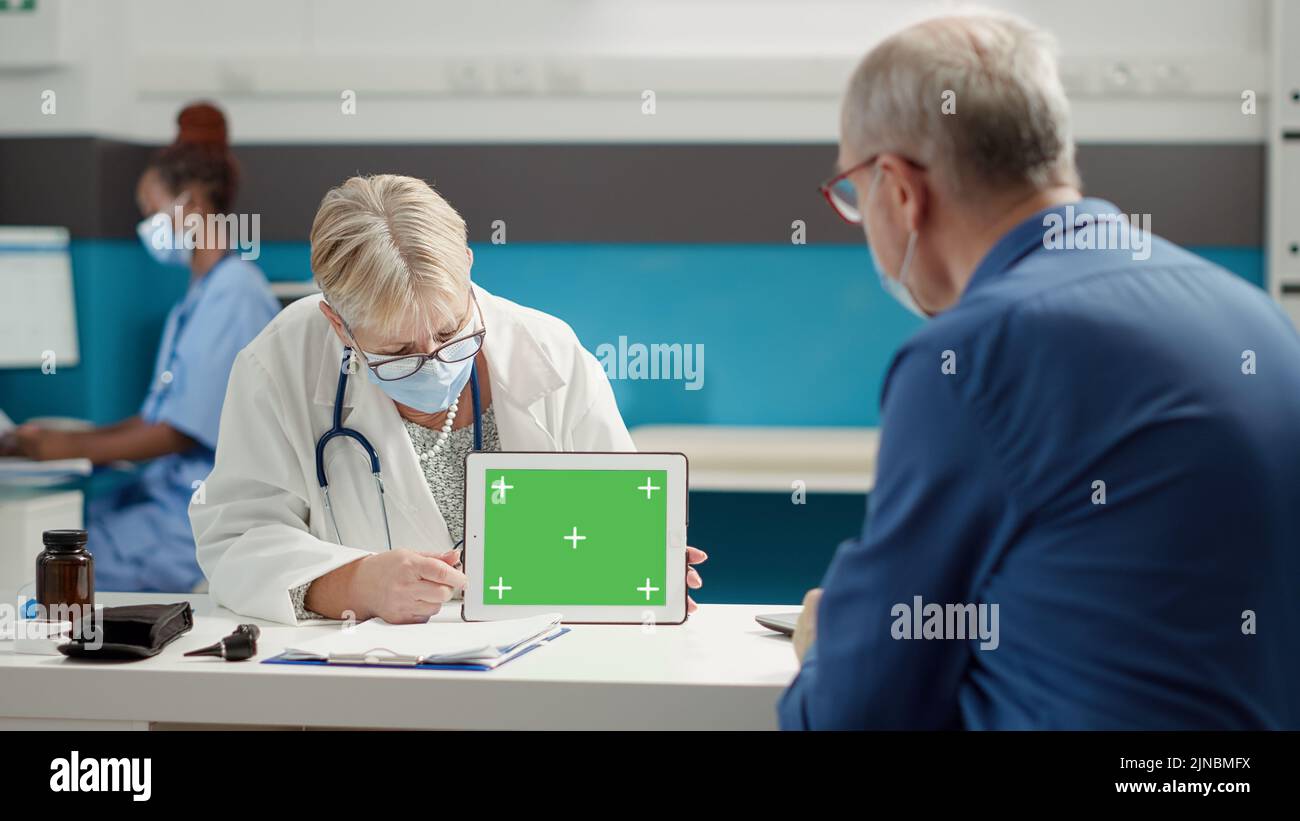 Doctor and retired person looking at greenscreen on tablet during covid ...