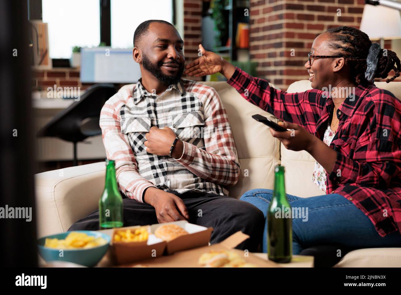 Young partners laughing and watching television together, eating fast ...