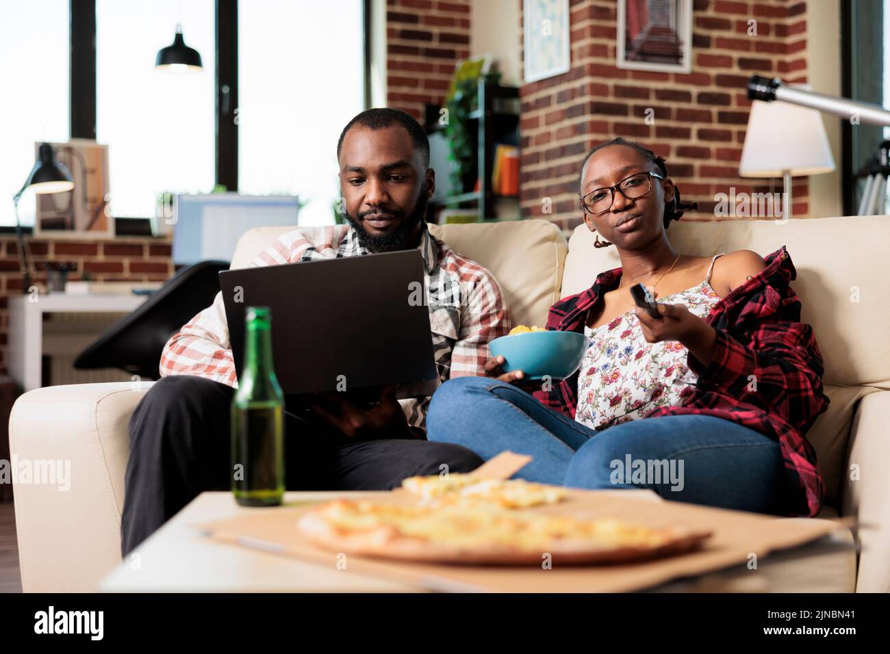 Boyfriend working on laptop and girlfriend switching tv channel, eating ...