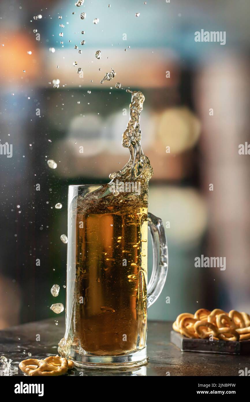 Glass mug of light cold beer with splash and flying drops with snacks ...