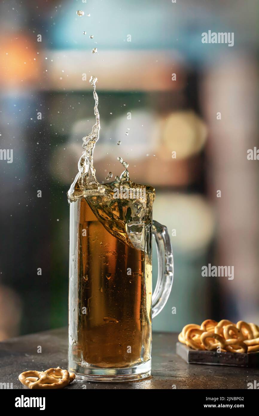 Glass mug of light cold beer with splash and flying drops with snacks ...