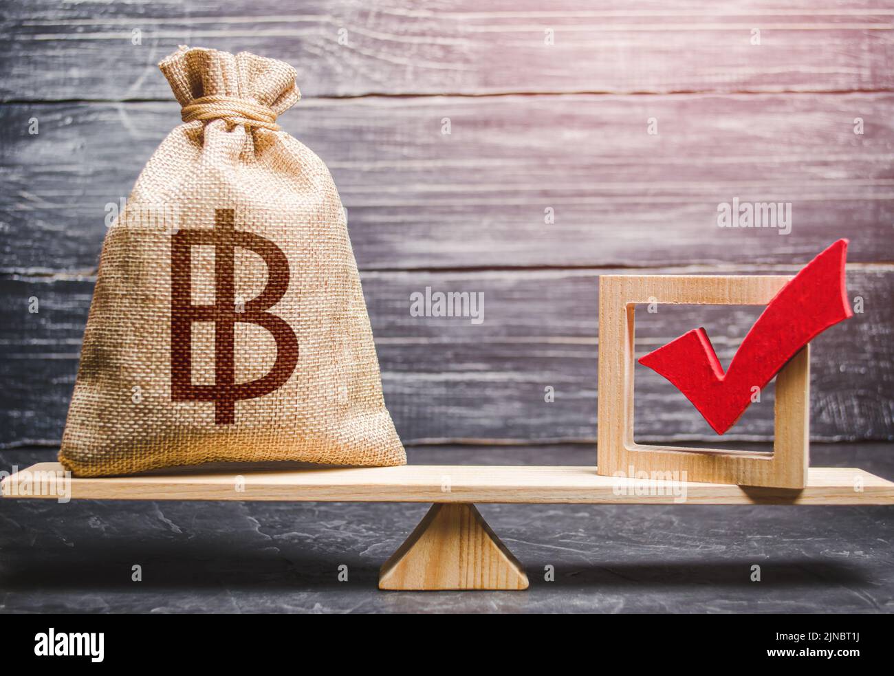 Red vote tick and a thai baht money bag on scales. Estimating cost of ...