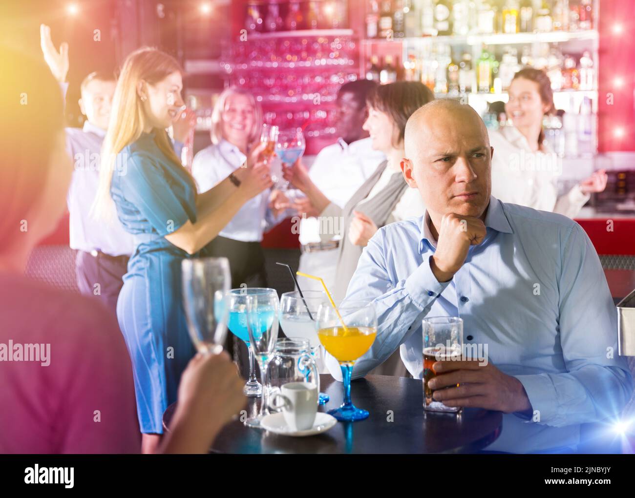Bored man sitting among dancing colleagues Stock Photo - Alamy
