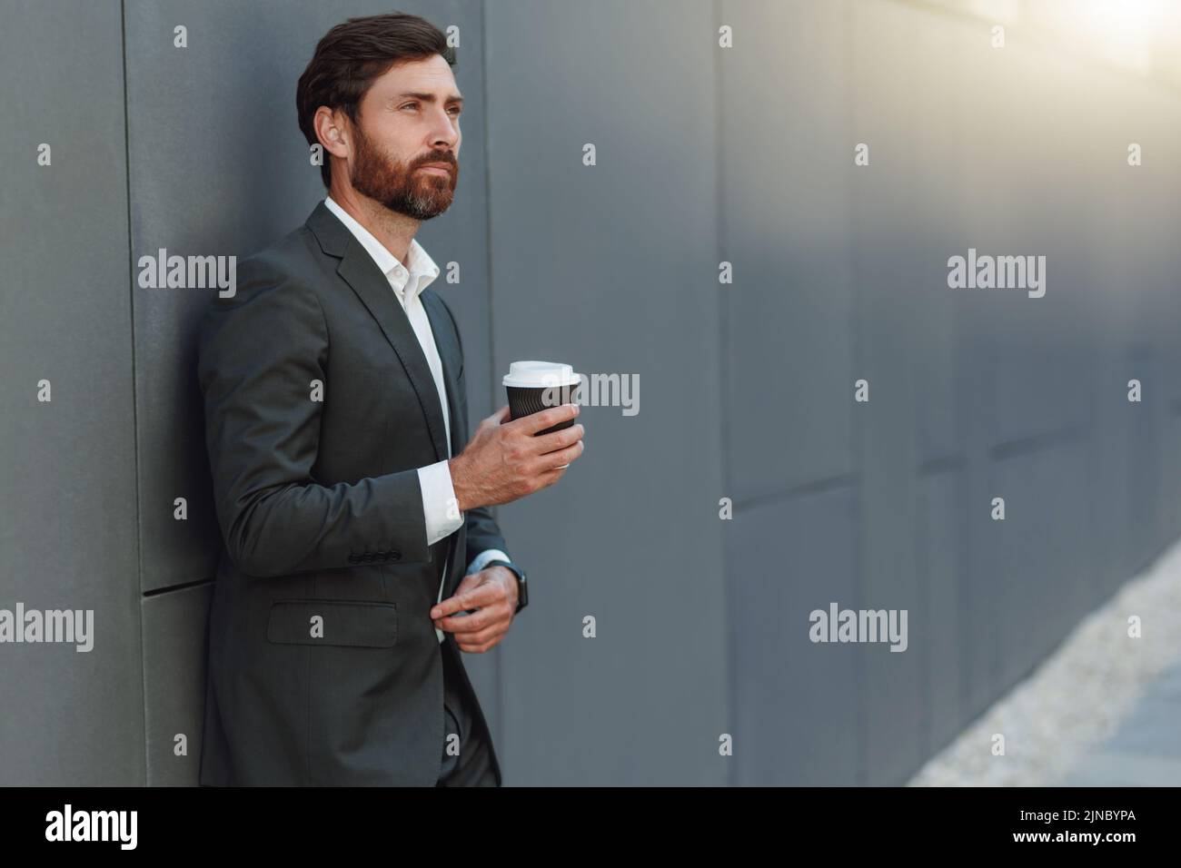 Focused european businessman in suit drinking coffee near office ...