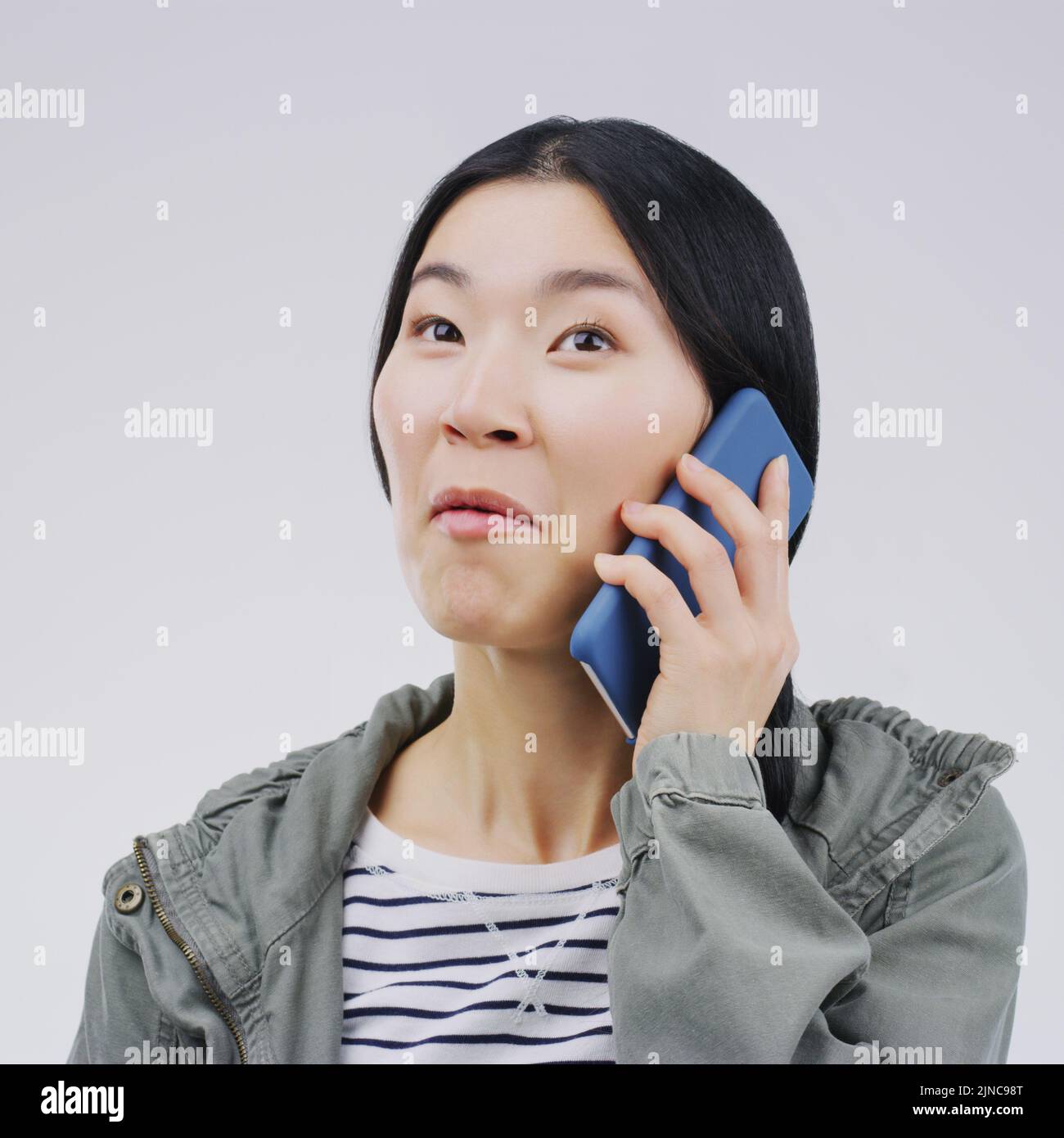 Have you heard. Studio shot of a young woman using a mobile phone against a grey background ...