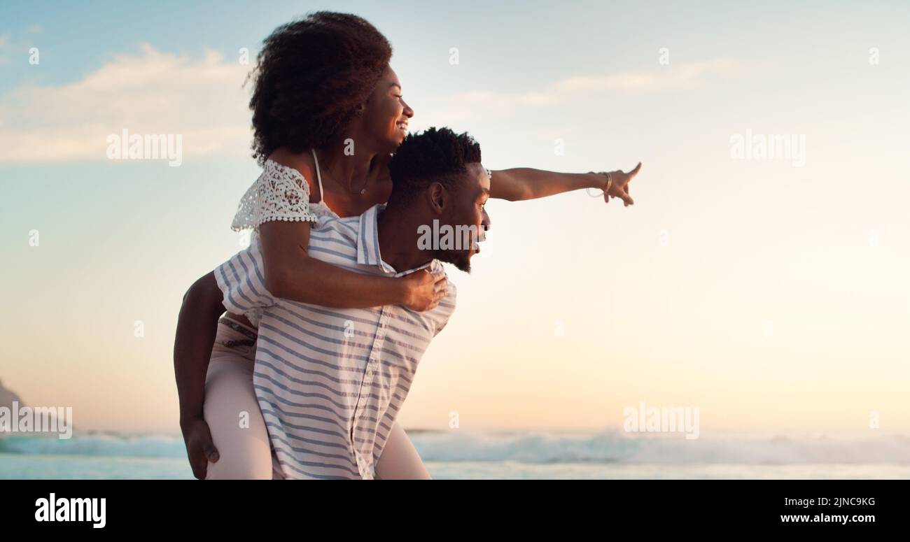 Lets head that way. a cheerful young woman being carried piggyback by ...
