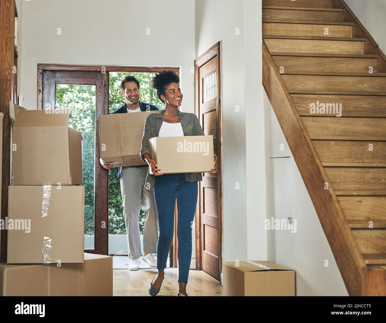 Interracial couple moving into a new modern house, carrying boxes and ...