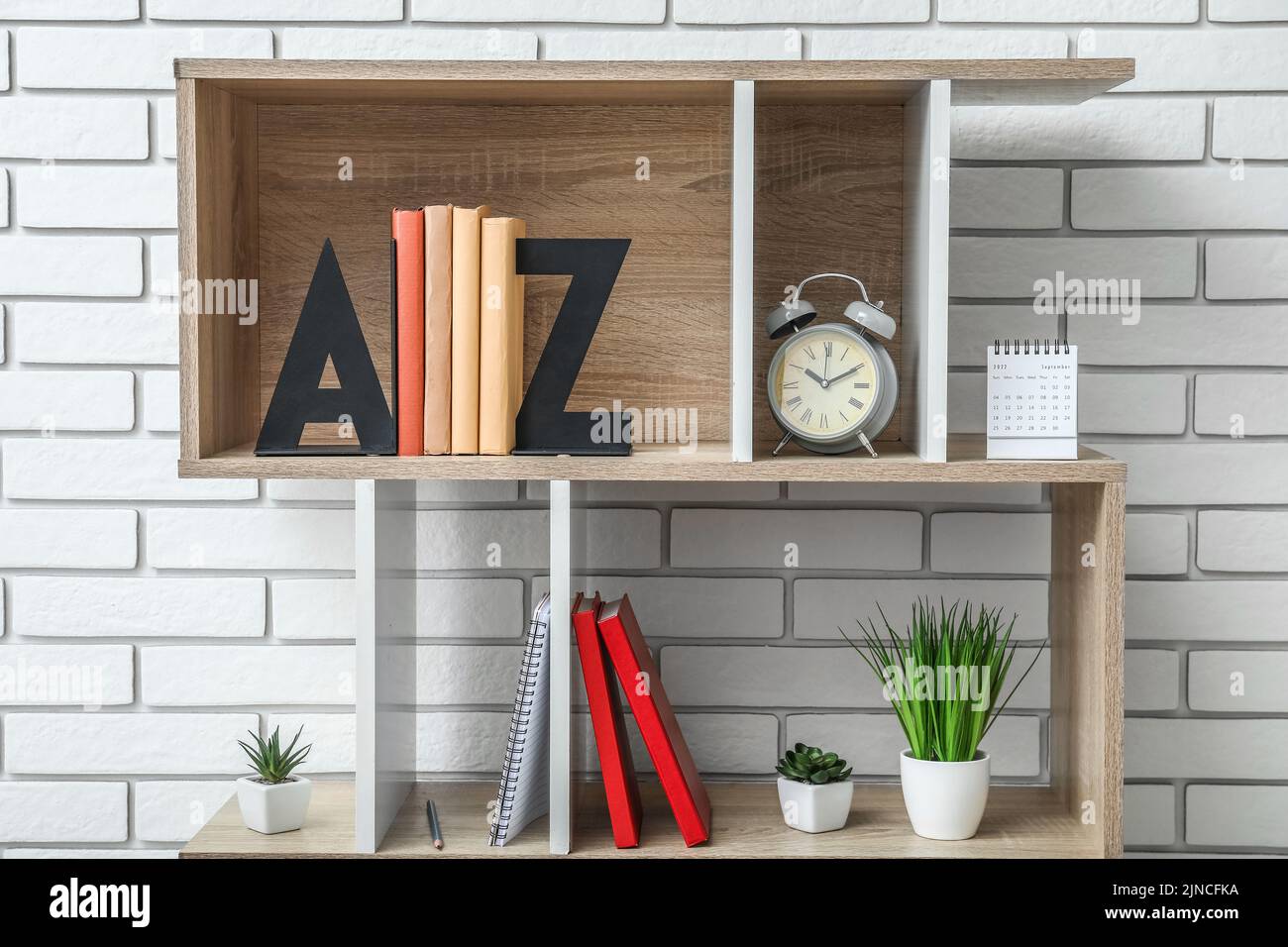 Bookcase with holder and alarm clock near white brick wall Stock Photo ...