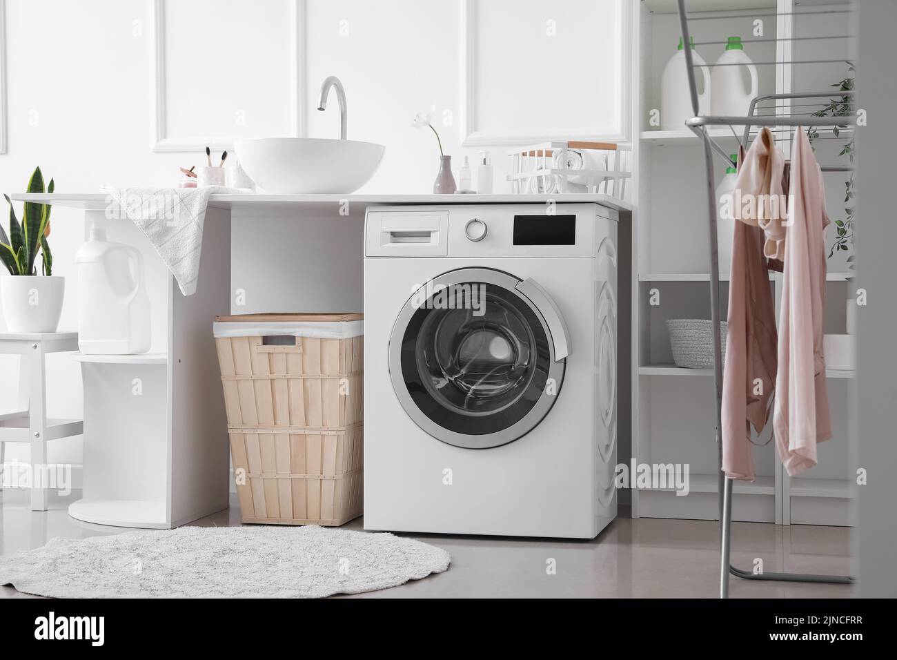 Table with sink, washing machine and basket near light wall in laundry ...