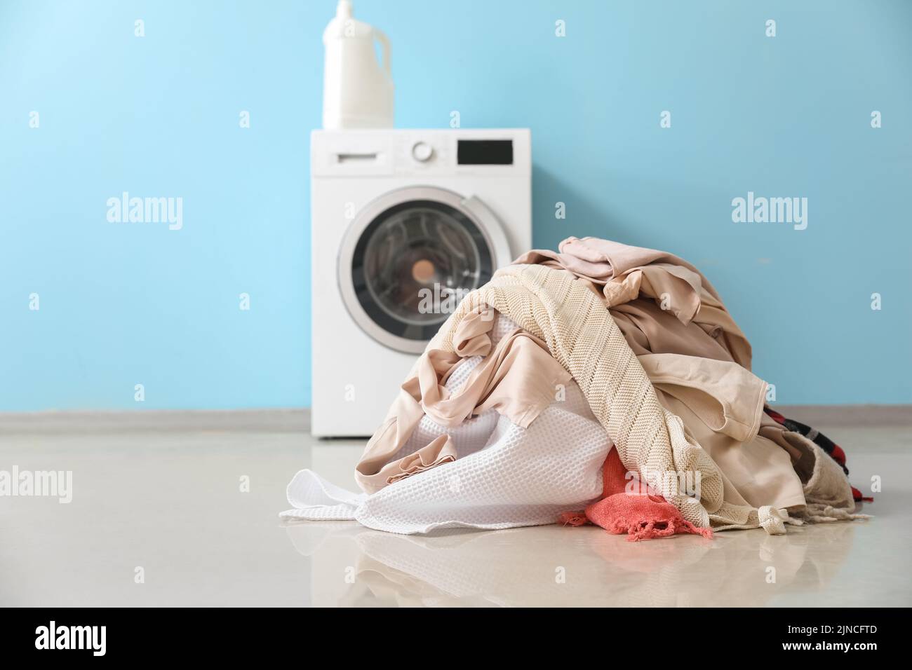 Stack of clothes and washing machine with detergent near blue wall ...