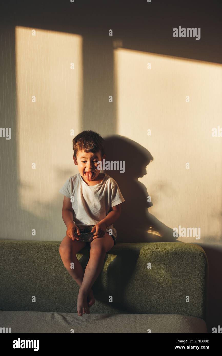 Boy eating from a bowl of blueberries sitting on the couch on the ...