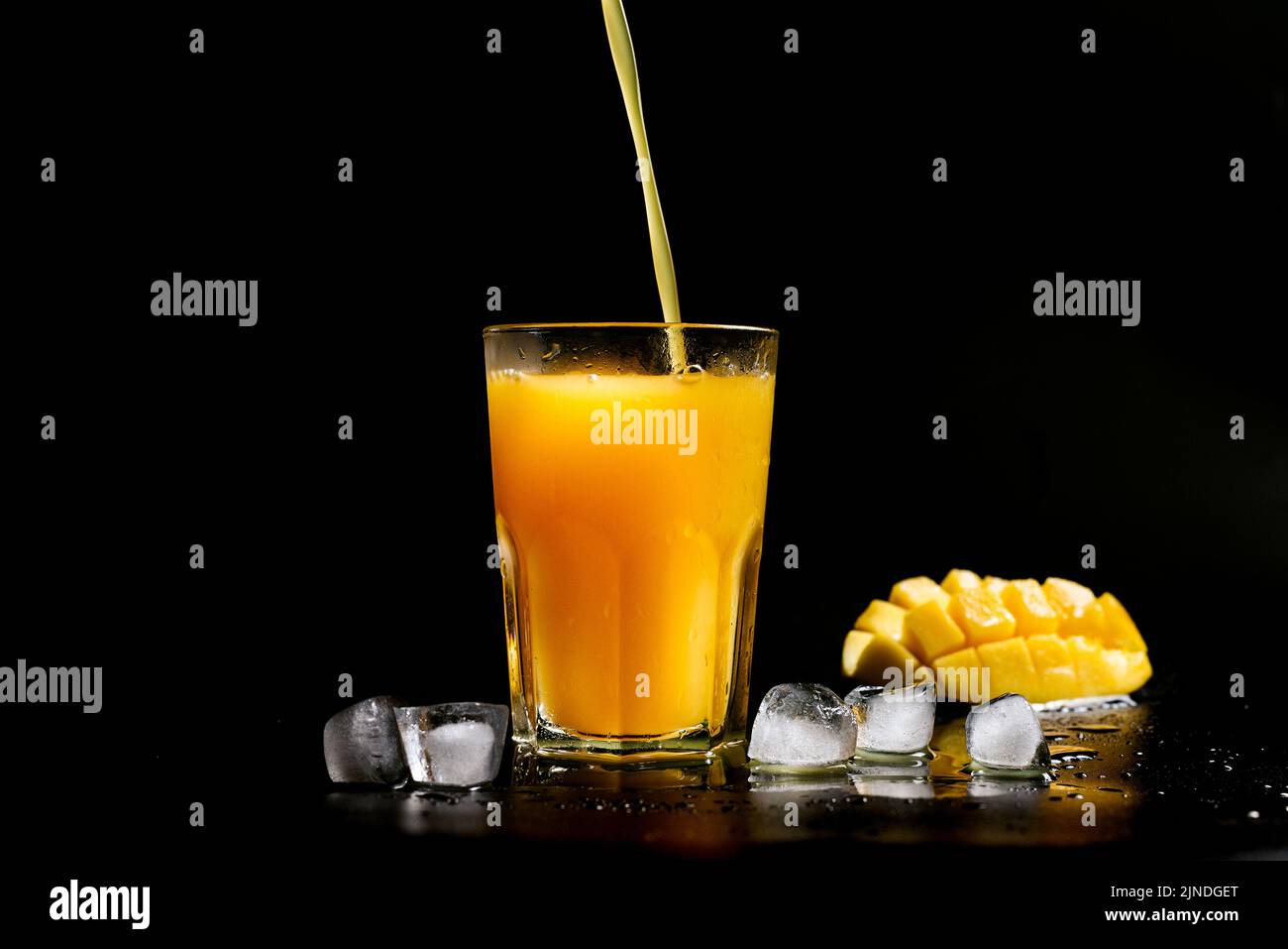 Fresh mango juice pours into a glass against a black background Stock ...
