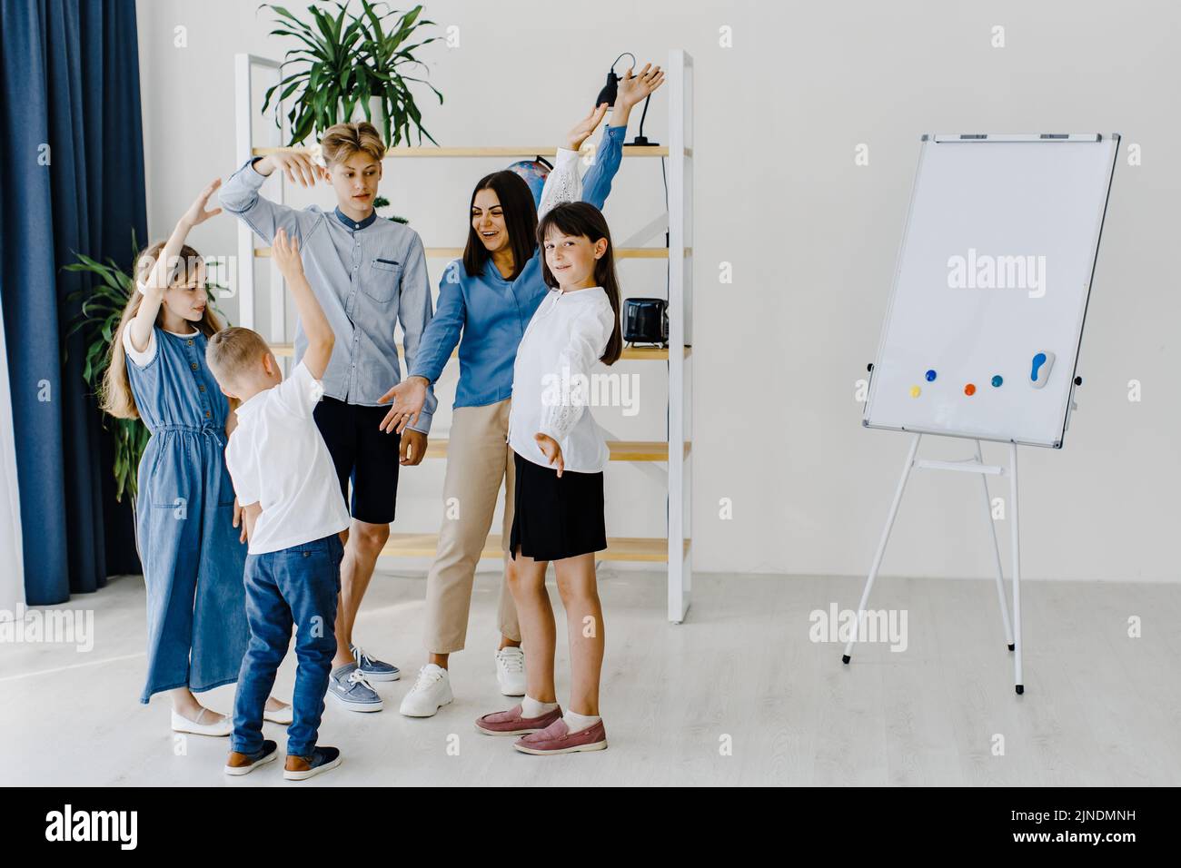 Happy children and educator raising hands up standing in modern ...