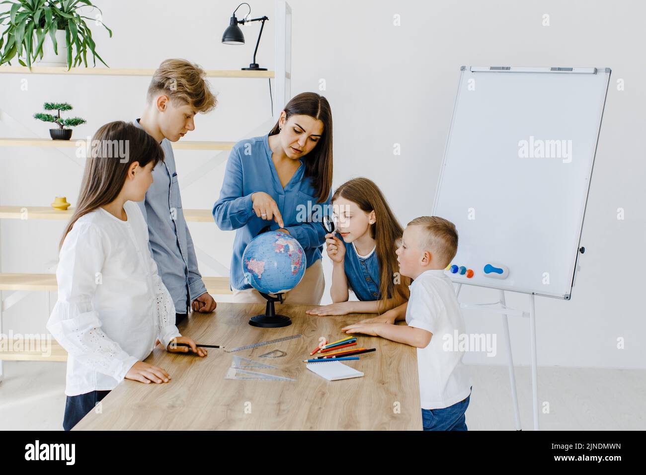Teacher and children in class are looking at globe, teacher helps ...