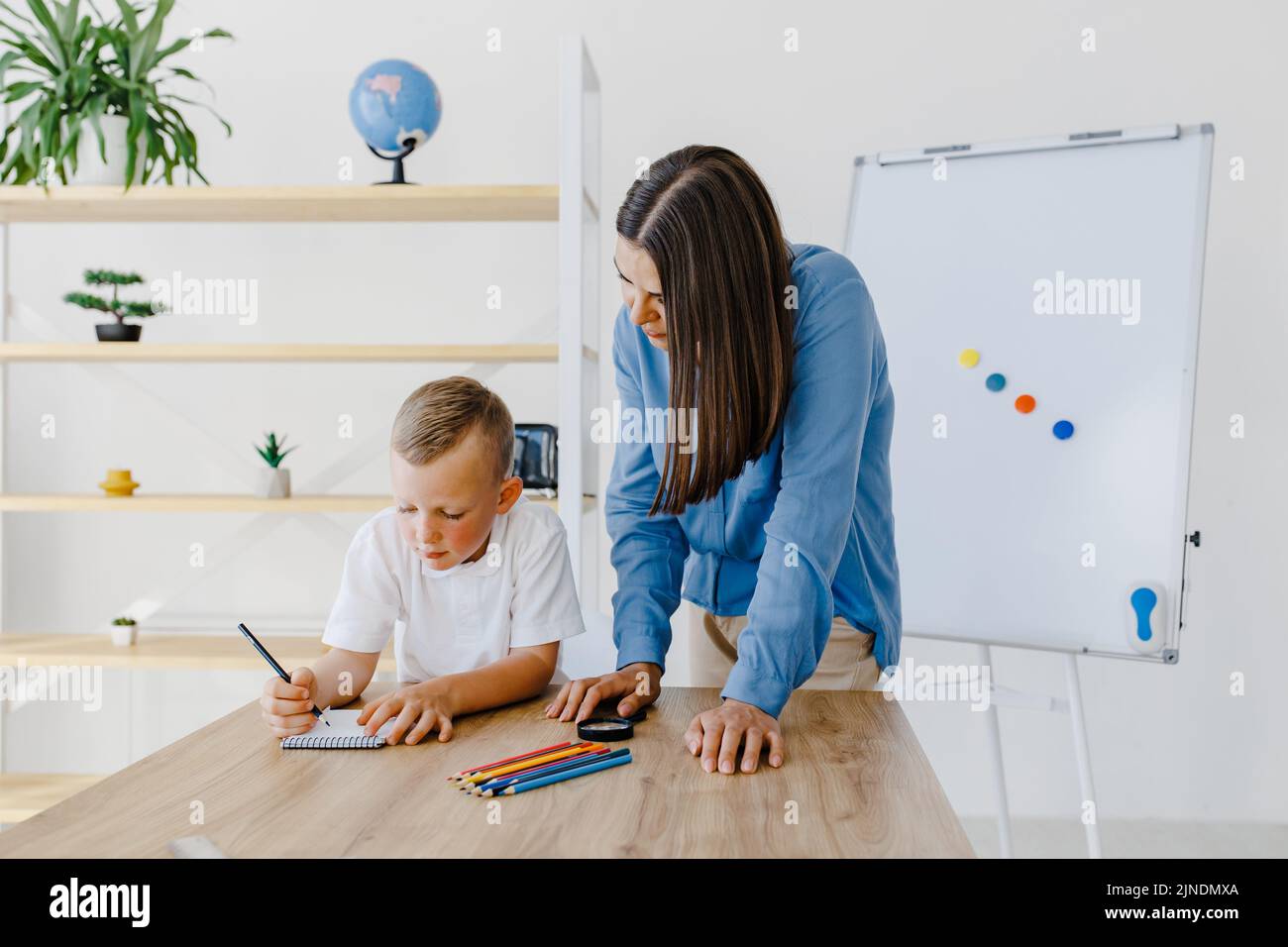 Private lesson. Attentive young woman tutor teacher helping little boy ...