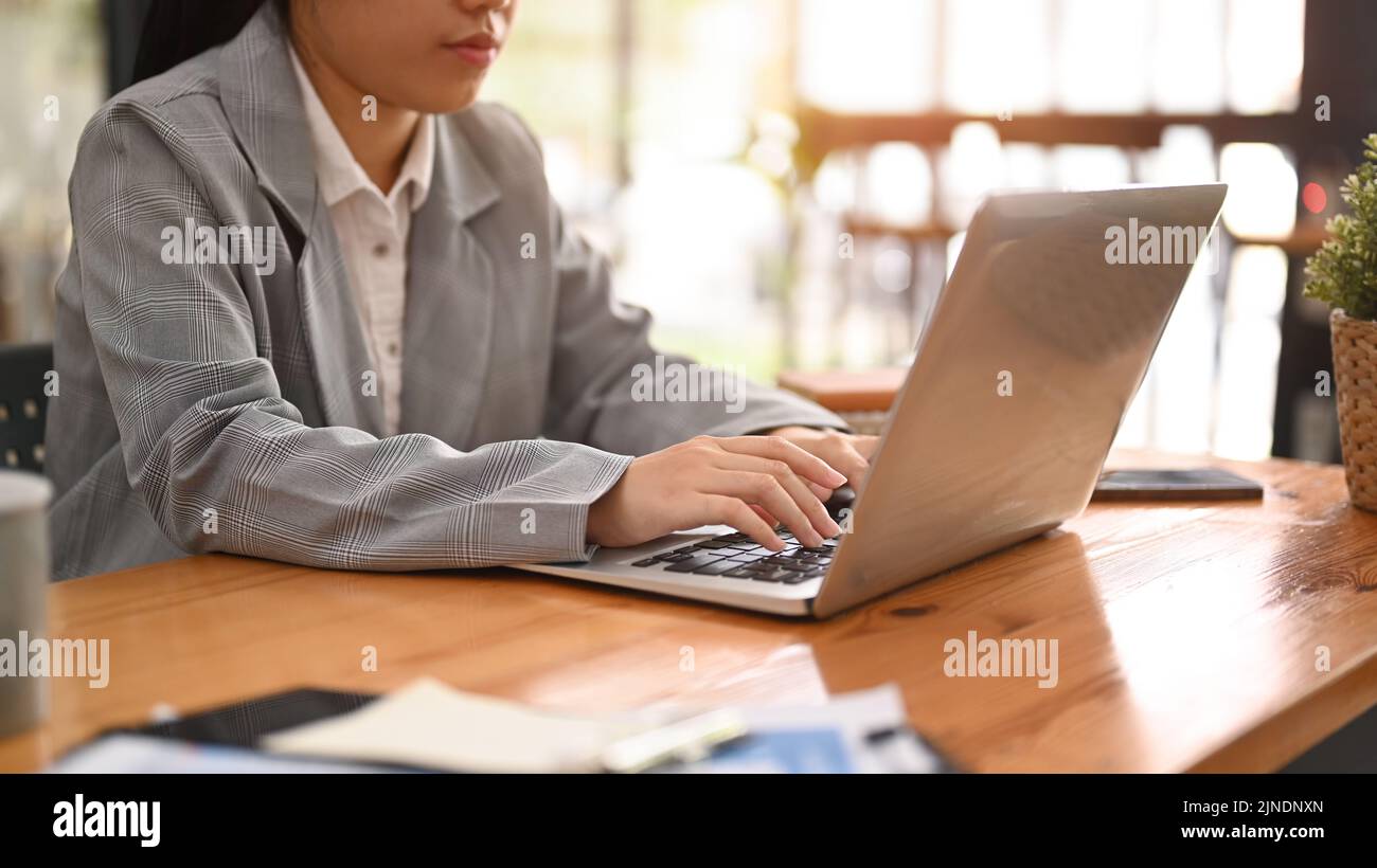 Young employee looking at screen, typing email on laptop at wooden ...