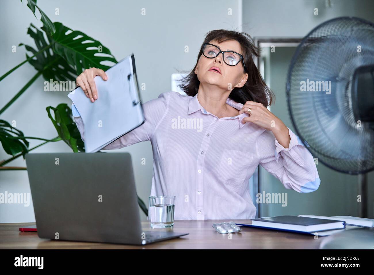 Middle-aged woman suffering from heat, overheated, cooled by fan and ...