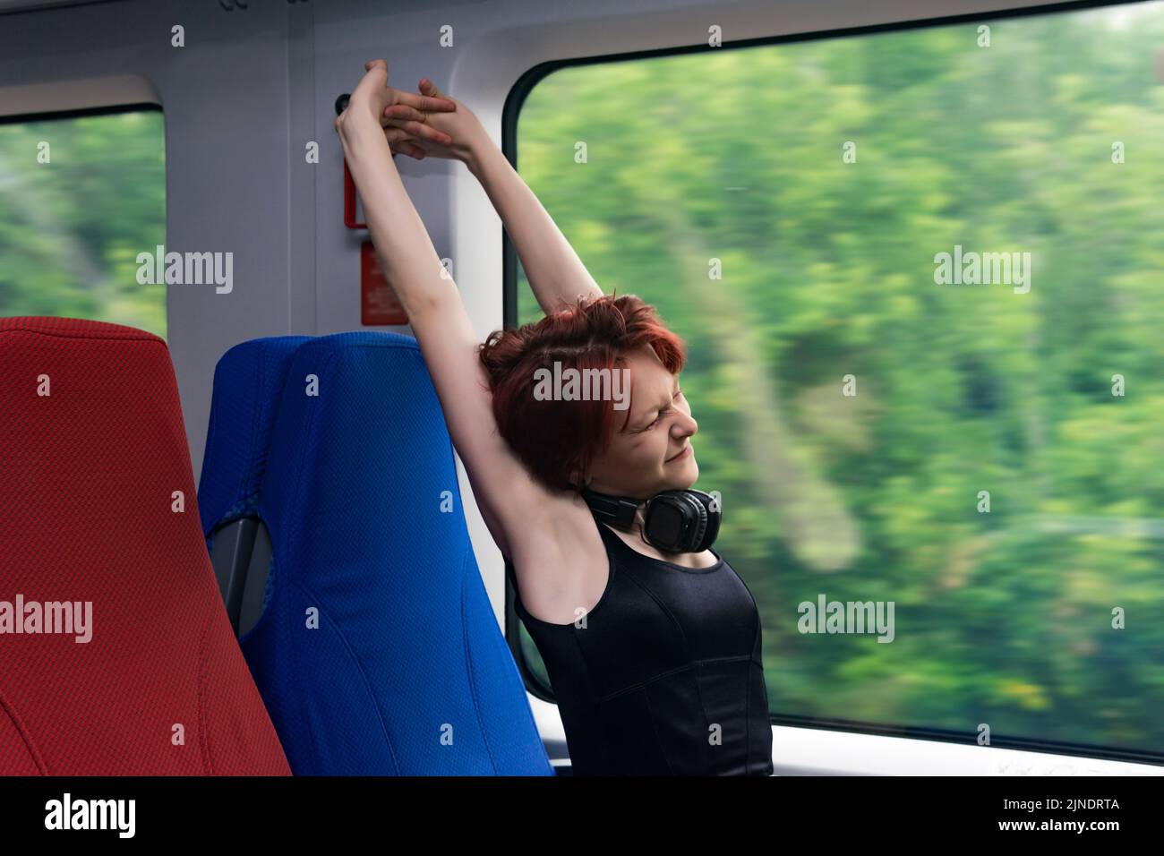 girl in a passenger train carriage is stretching, tired from a long ...