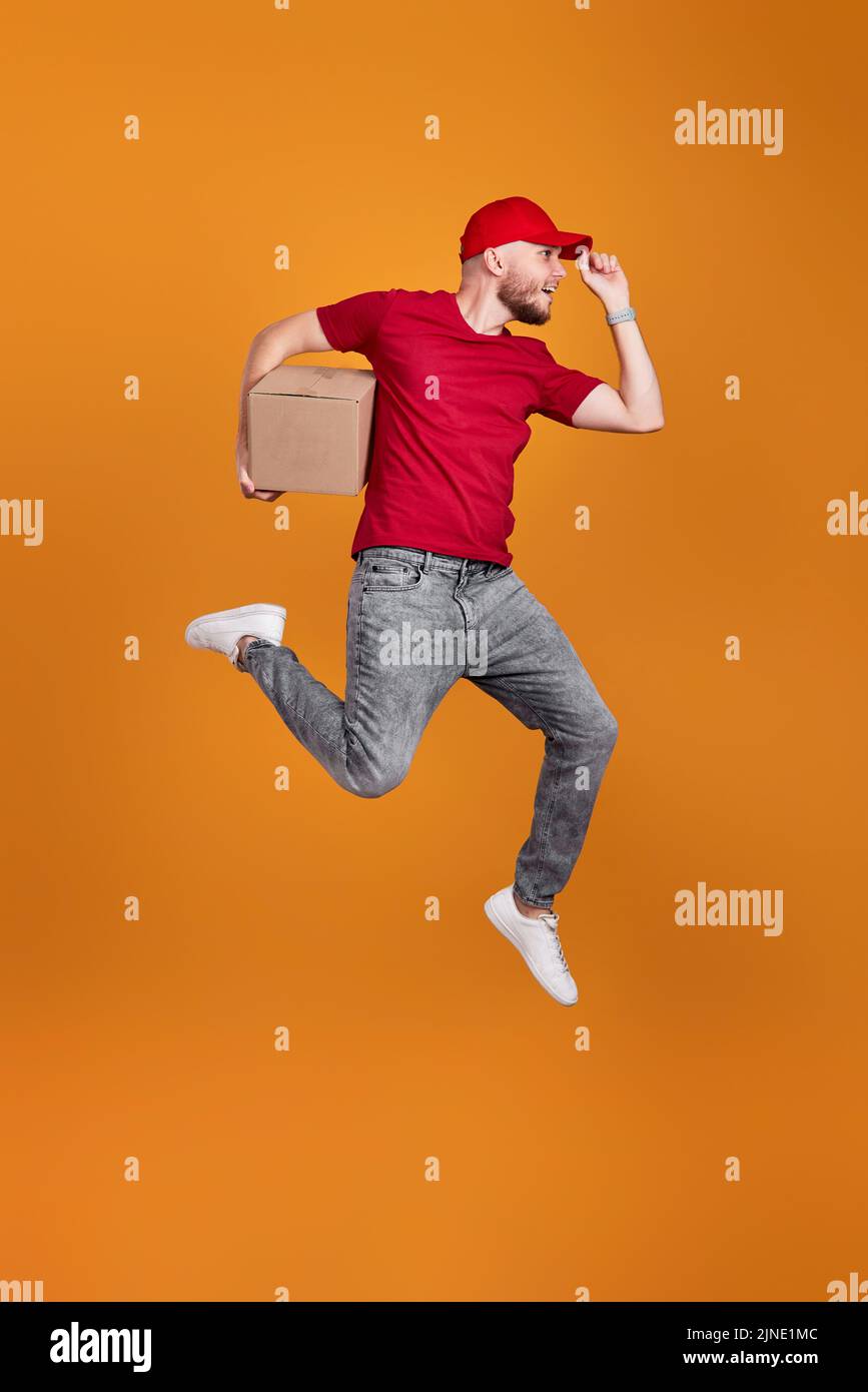 Delivery man in red cap holding cardboard box and jumping Stock Photo ...
