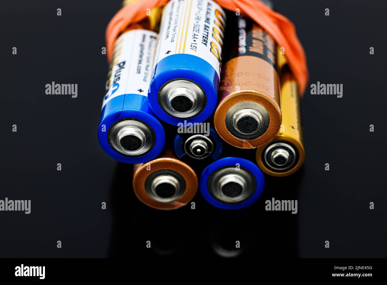 A collection of AAA and AA batteries tied with rubber band on black ...