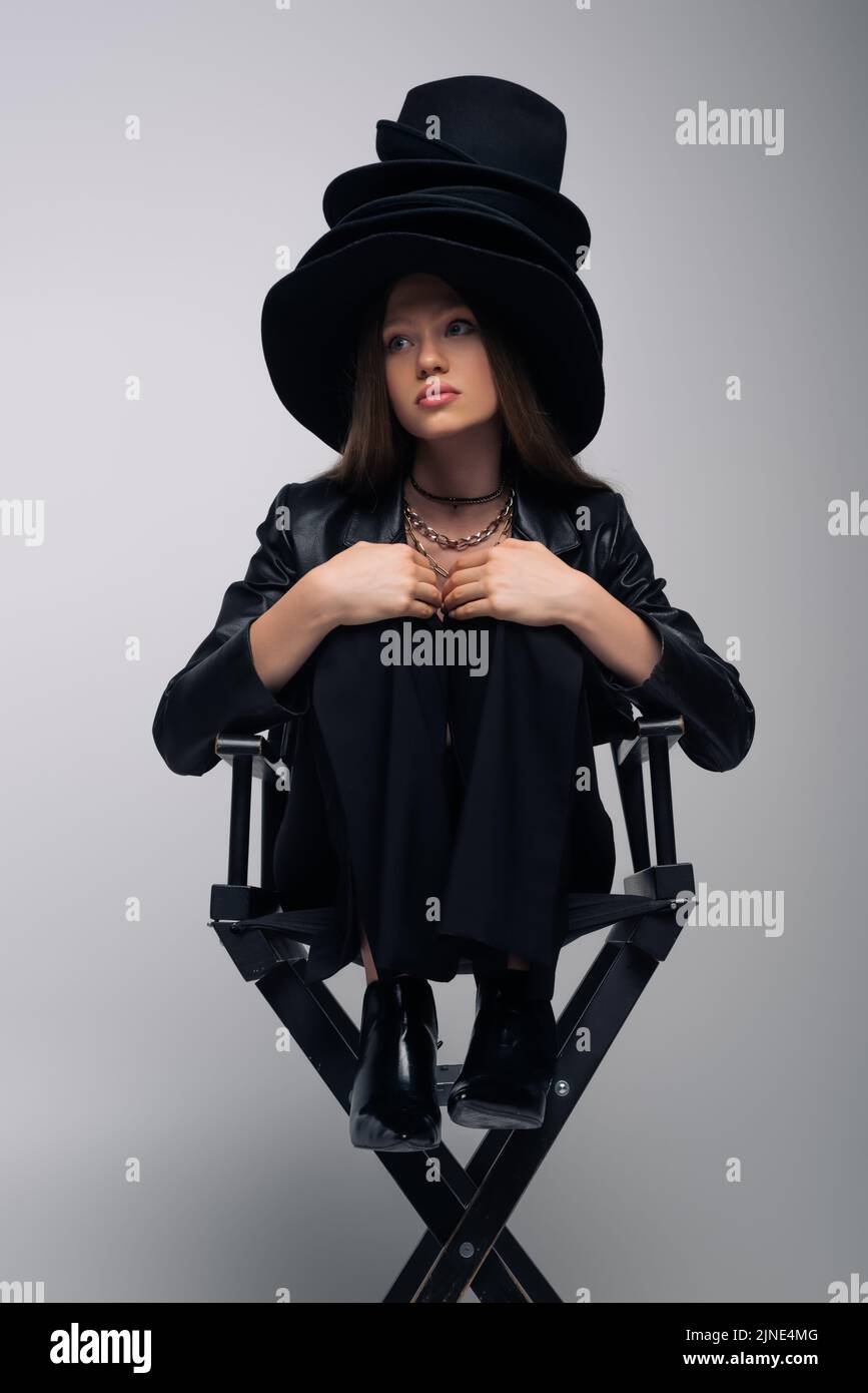 model in black leather jacket and different black hats sitting on chair ...