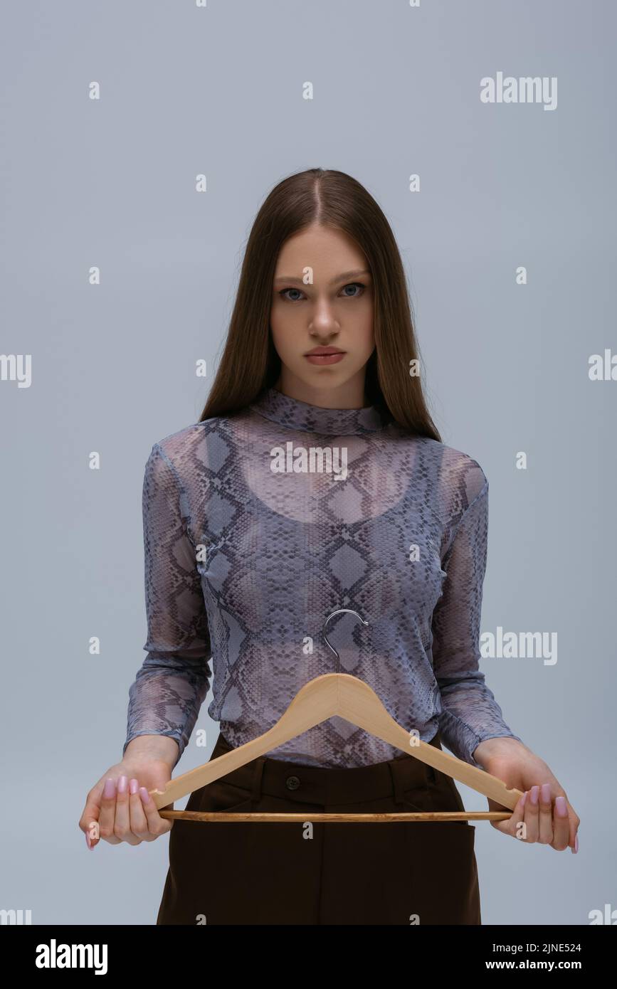 brunette teenage model holding wooden hanger standing isolated on grey ...