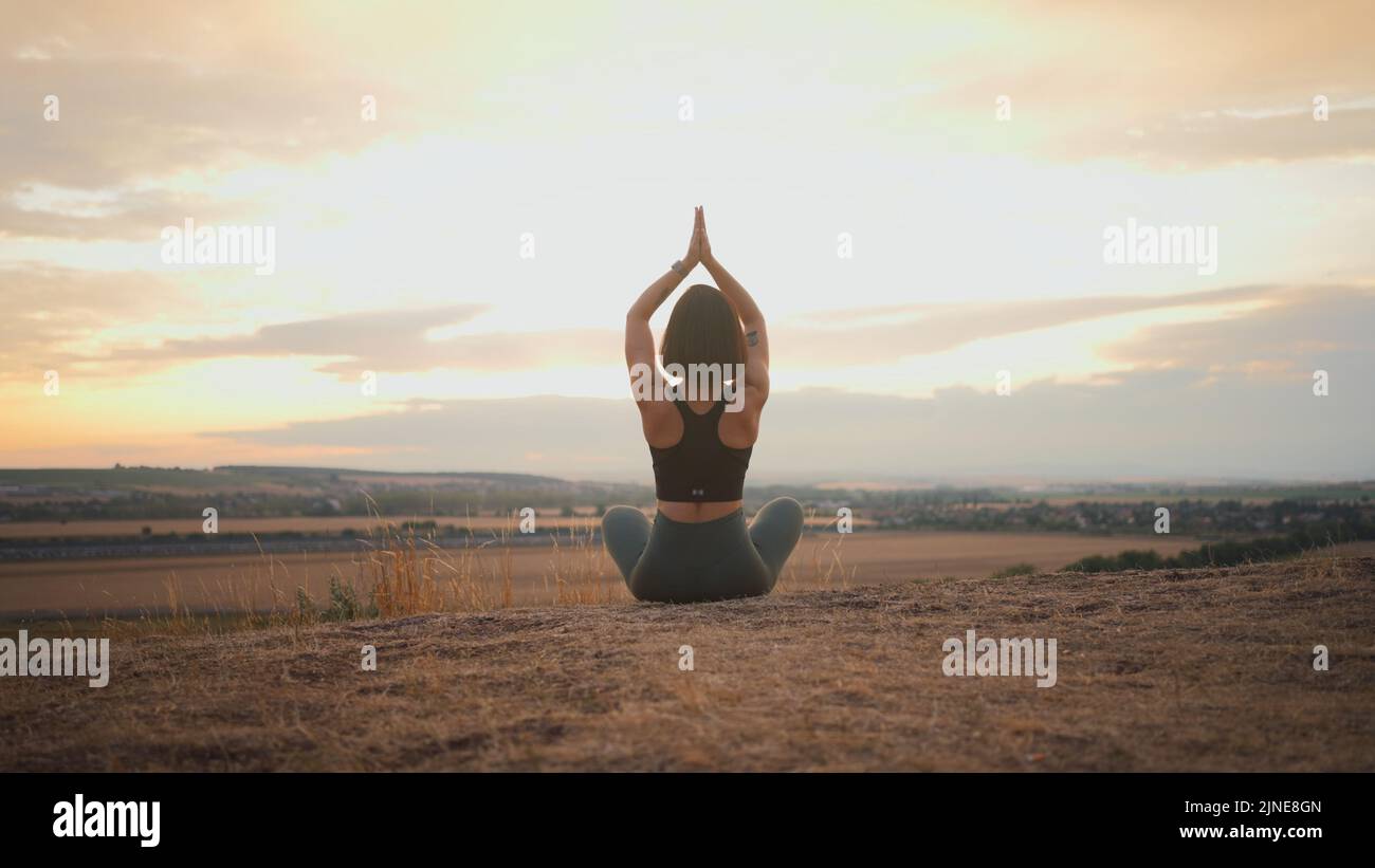 Back view of serene young woman enjoying meditation at the evening ...