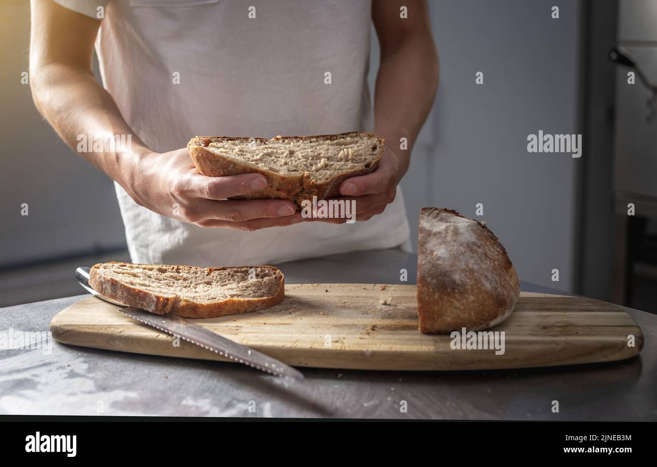 A male baker cuts freshly baked bread with a knife to check the quality ...