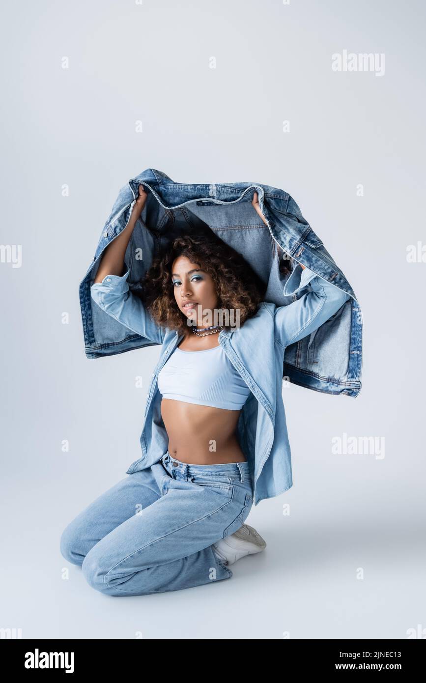 african american woman with denim jacket sitting on haunches on grey ...