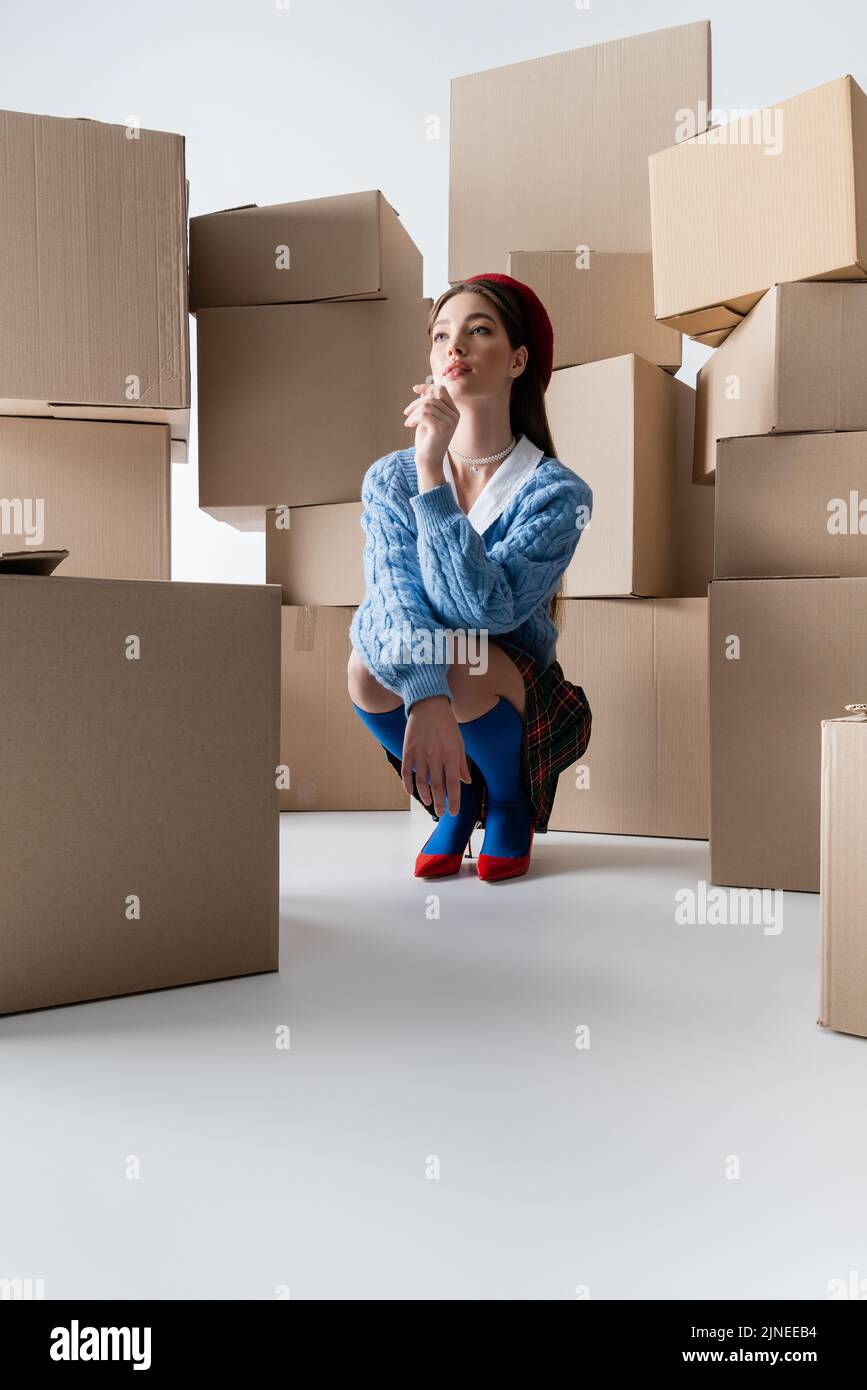 Trendy model in knitted cardigan posing near cardboard boxes on white ...
