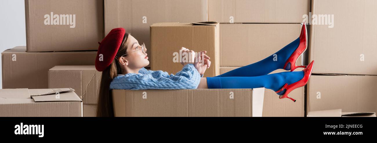Side view of stylish woman sitting in cardboard box on white background ...