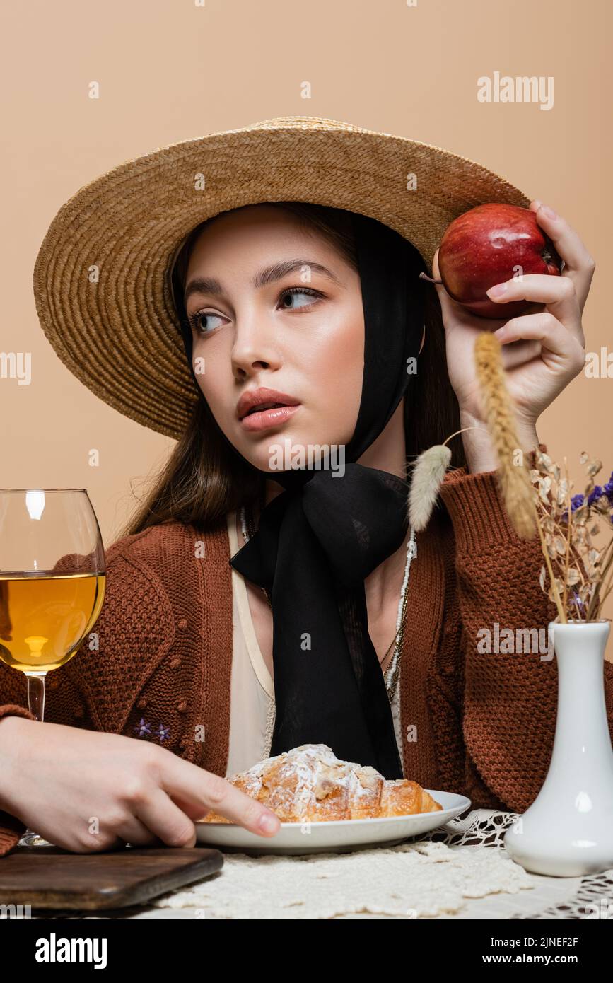 Stylish model holding apple near croissant and wine on table isolated ...